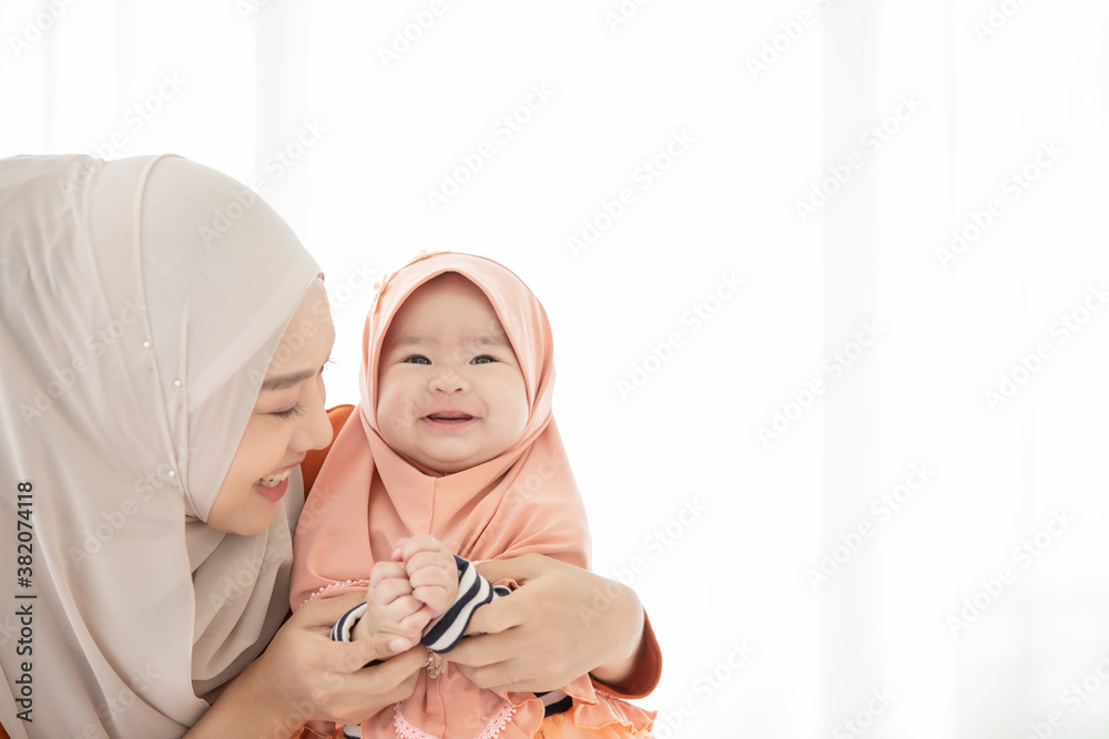 A Muslim mother and toddler are indoors in their bedroom. The mother is ...