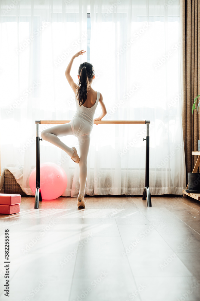 Portrait of cute little girl practicing ballet and standing at barre at ...