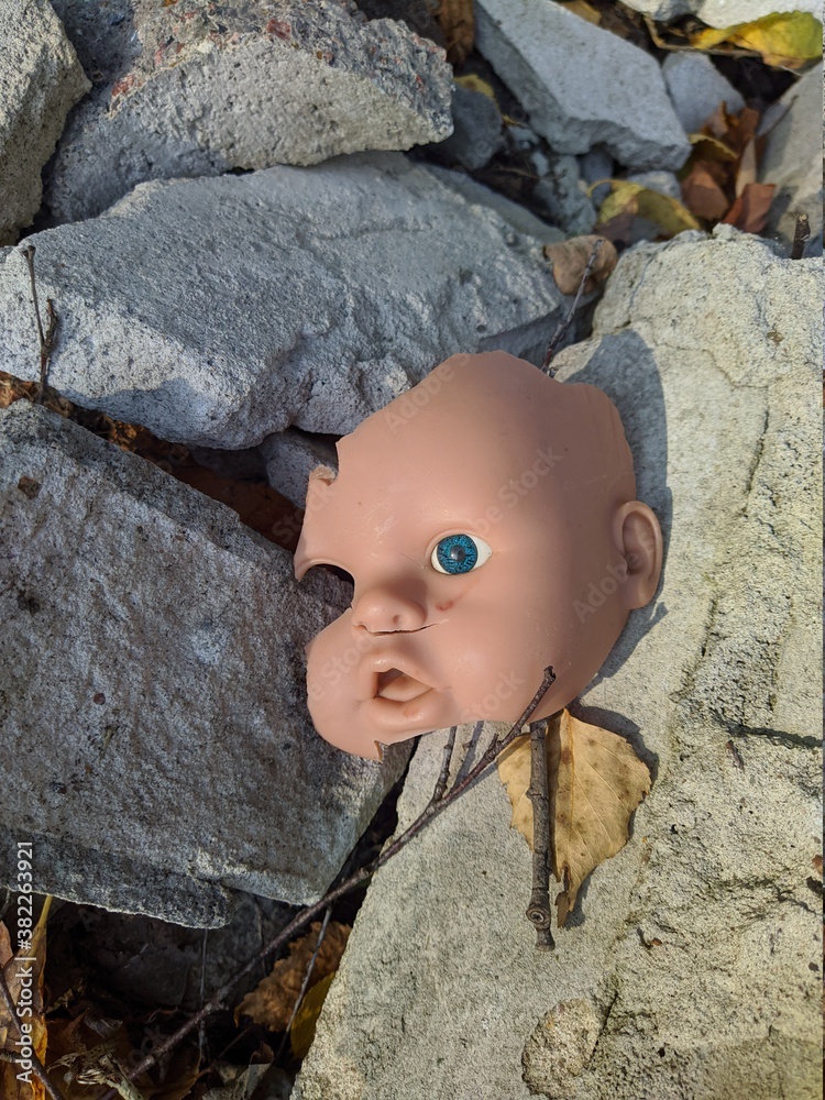 scary and broken doll face with one blue eye on a background of stones ...