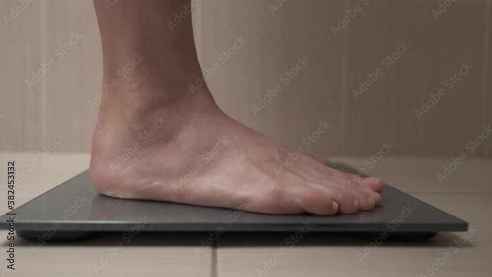 Unrecognizable barefoot woman steps on bathroom scales and measure ...