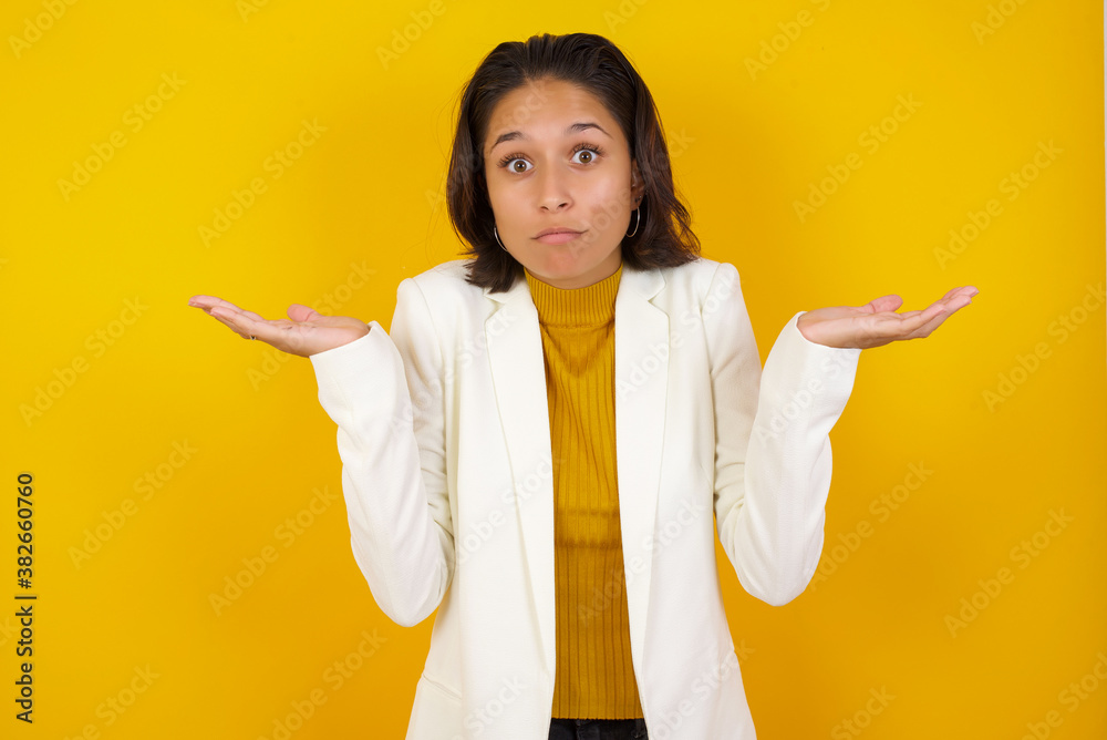 Puzzled and clueless young woman with arms out, shrugging her shoulders ...