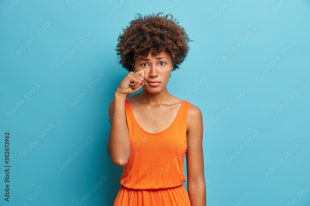 Disappointed dejected dark skinned curly woman wipes tears stands ...