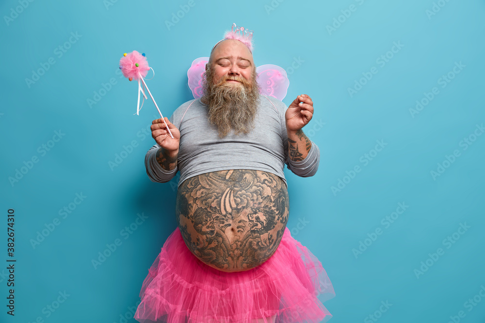 Funny bearded adult man in fairy costume closes eyes in pleasure holds ...