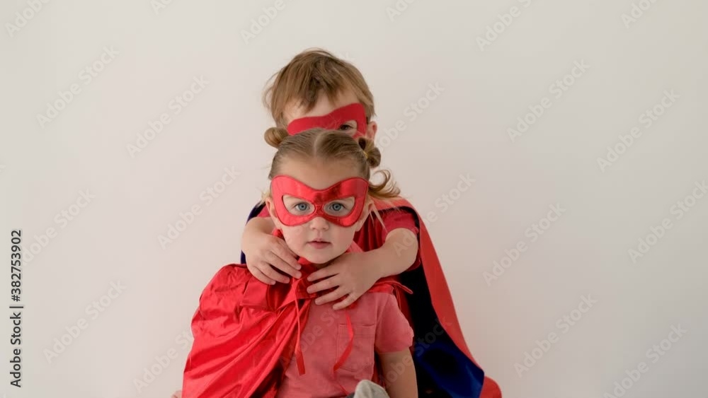 Funny boy in coloured superhero costume hugs and kisses little sister ...