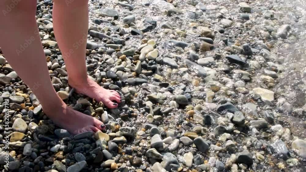 Female Legs With Bright Black Pedicure On Pebble Beach Being Washed By