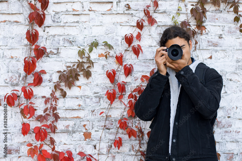 Outdoors shot of a young man in black coat with dslr camera in his ...