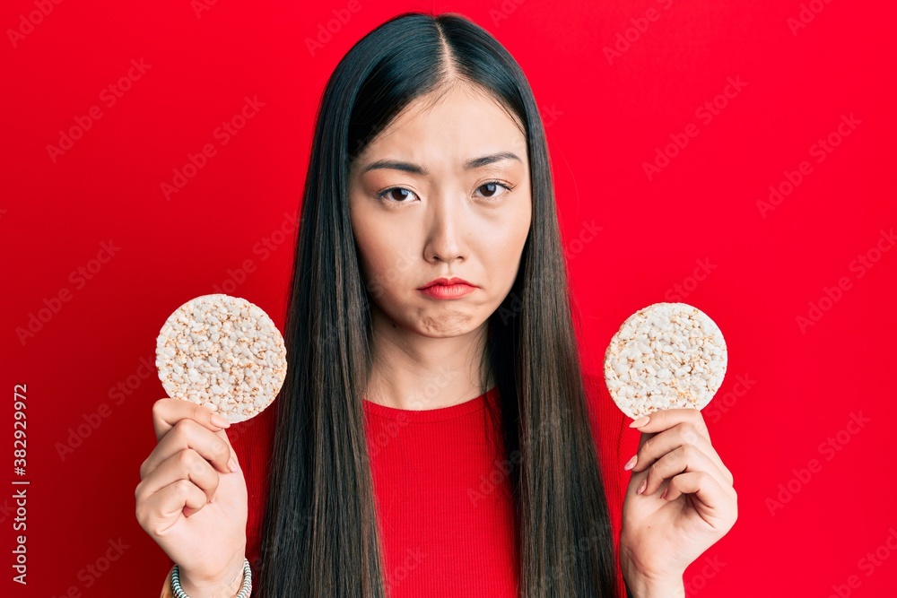 Young chinese woman eating healthy rice crackers depressed and worry ...