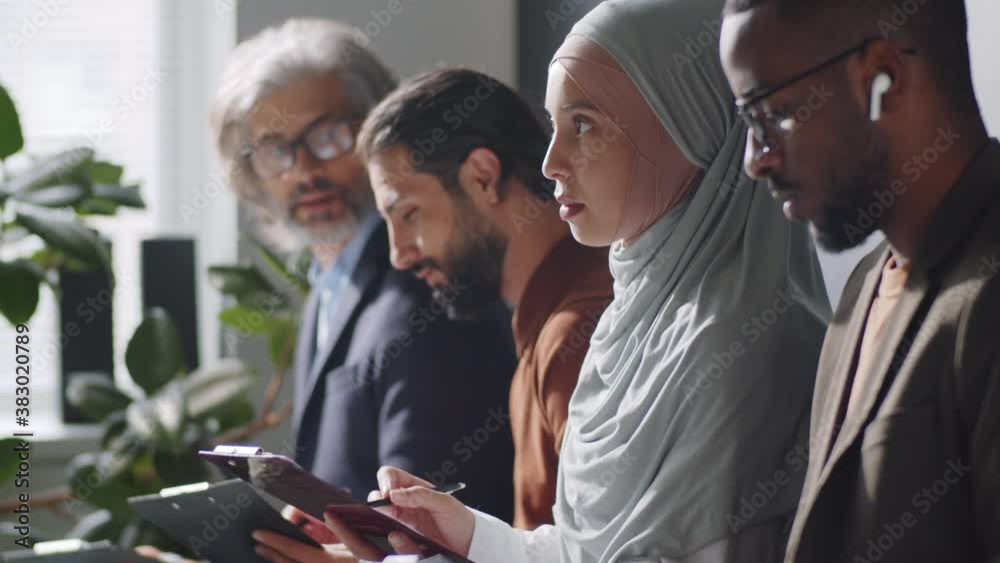Tilt up shot of young muslim woman in hijab sitting with diverse male ...