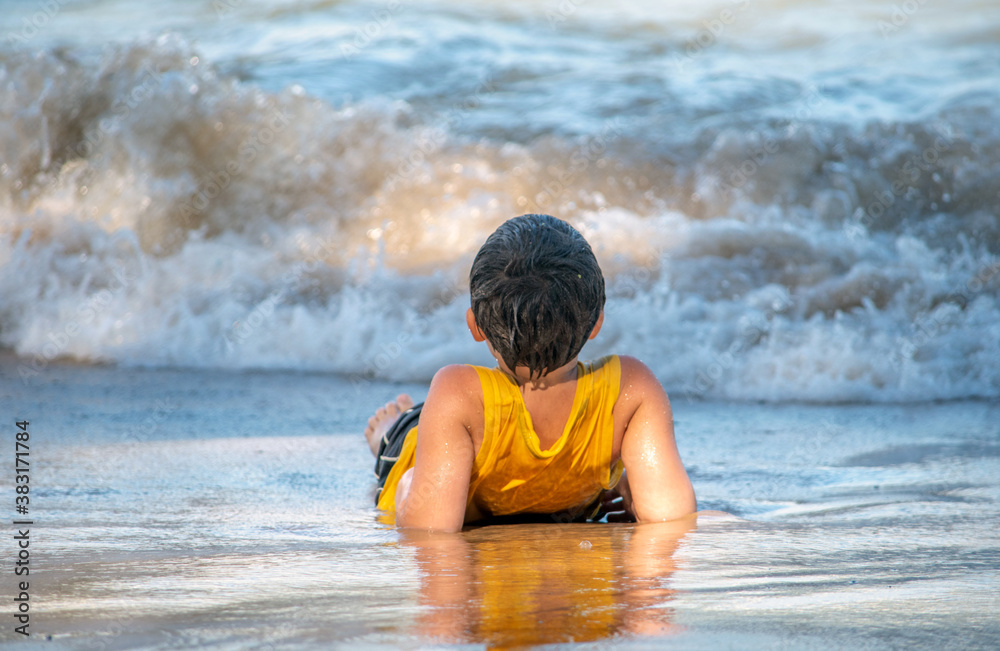 Young boy is a wave watcher, as he lies on the beach and watches the ...