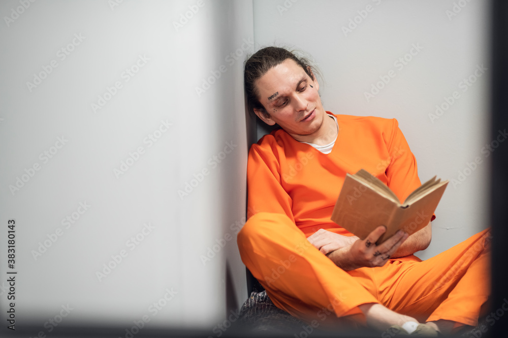 Stockfoto A dangerous mad criminal reads a book sitting on a bunk. In ...