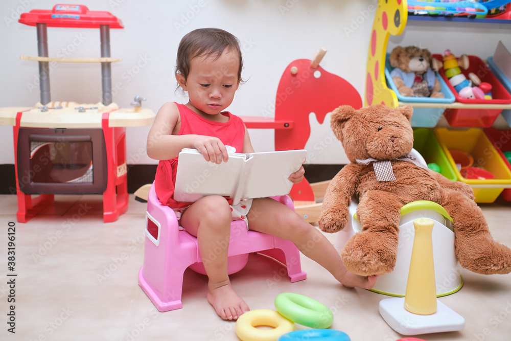 Asian toddler girl child sitting on potty and reading a book with toys ...