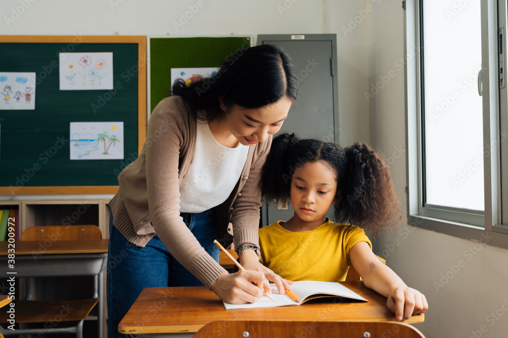 Asian school teacher assisting female student in classroom. Young woman ...