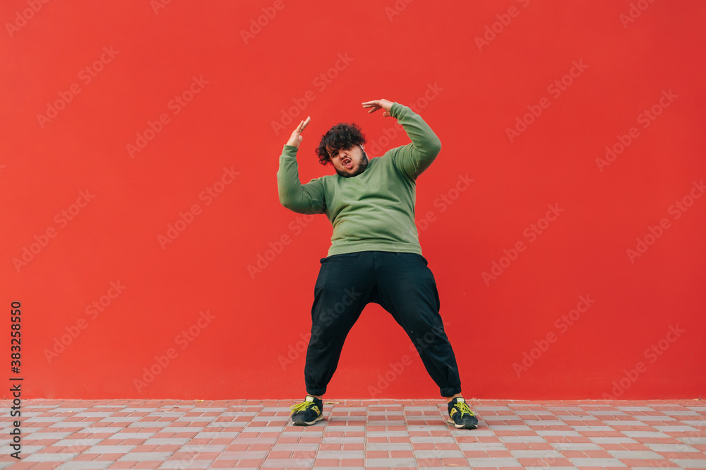 Foto de Funny fat guy in casual clothes dances on a red wall and looks ...
