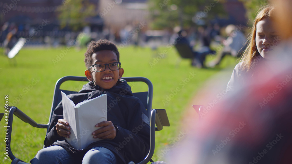 Curious kids sitting with workbooks on folding chairs while listening ...