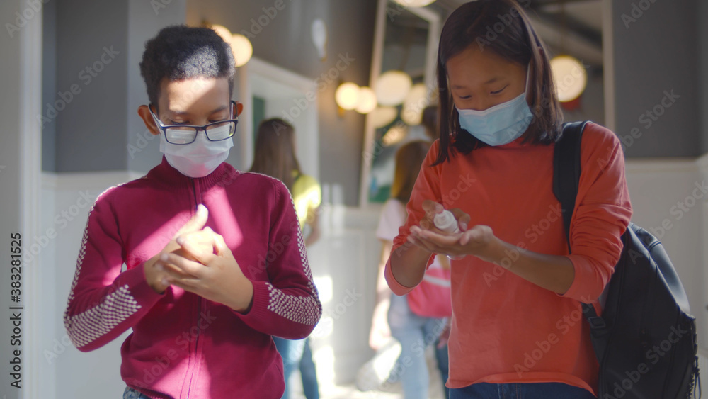 Multiethnic schoolchildren in safety mask disinfecting hands with ...