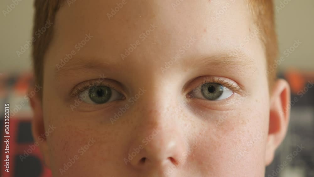 Close up blue eyes of small red-haired boy blinking and looking into ...