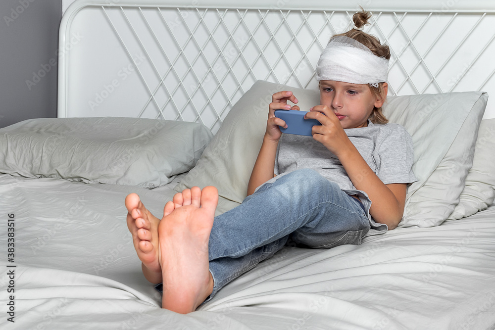 Little Caucasian blond boy with a head injury and bandage is lying on ...