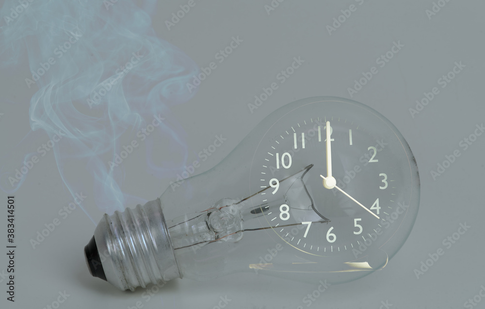 Abstract a light bulb with soot from working and a black analog clock ...