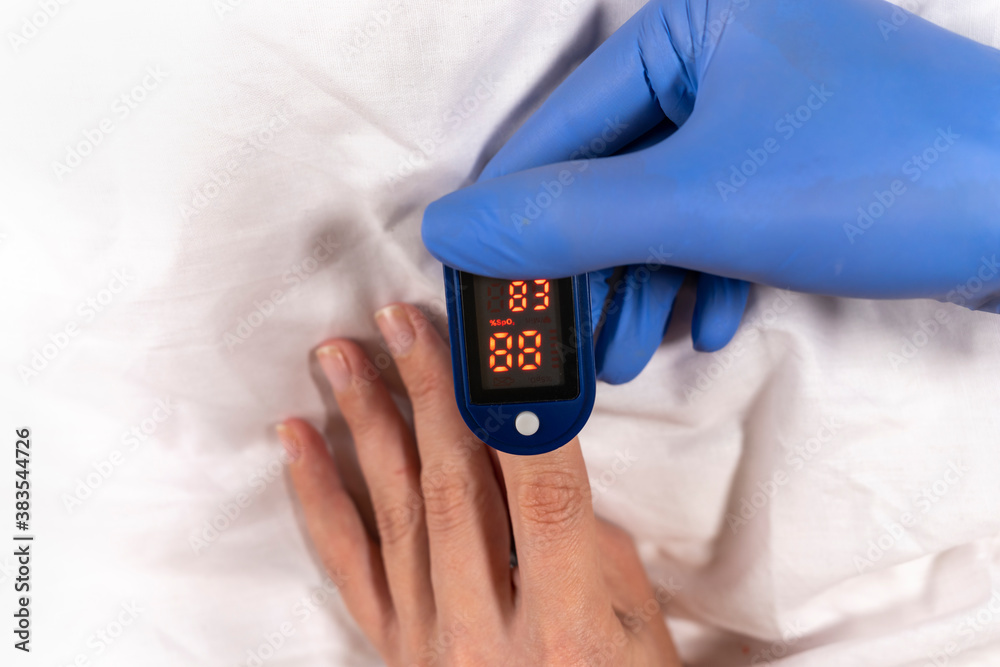 A gloved doctor measures oxygen in the blood of a patient with ...