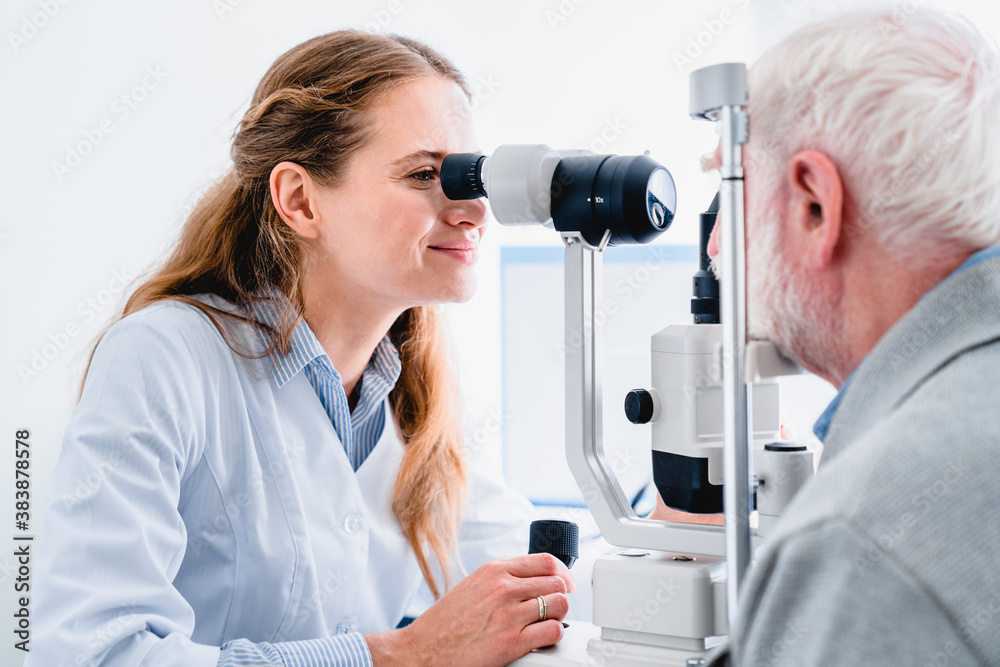 Smiling young female oculist checking senior patient`s vision with ...