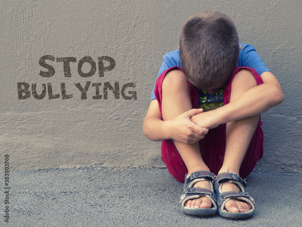 Sad boy hides his face between his knees sitting on the floor. Stop ...