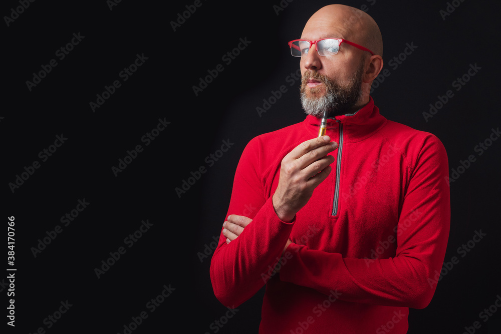 Bald man in his 40s with grey beard holding e-cigarette in his hand and ...
