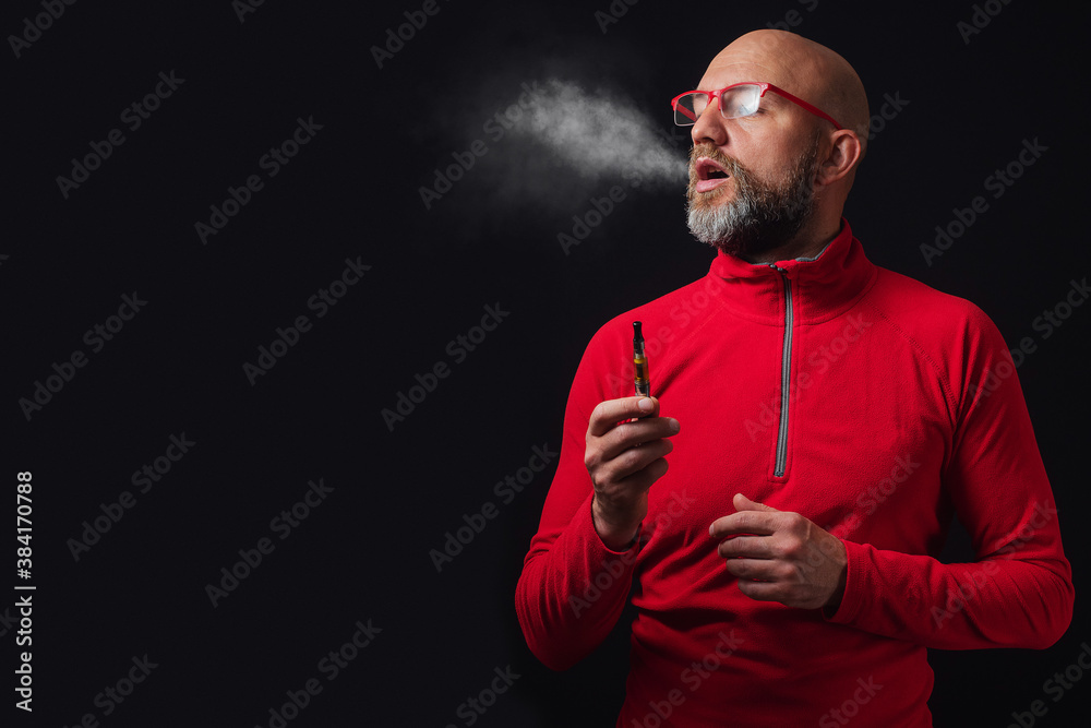 Bald man in his 40s with grey beard holding e-cigarette in his hand and ...