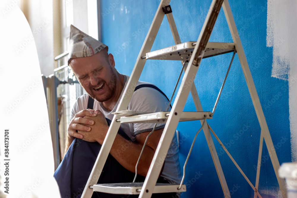 Craftsman sitting next to the ladder with pain in the knee. Knee injury ...