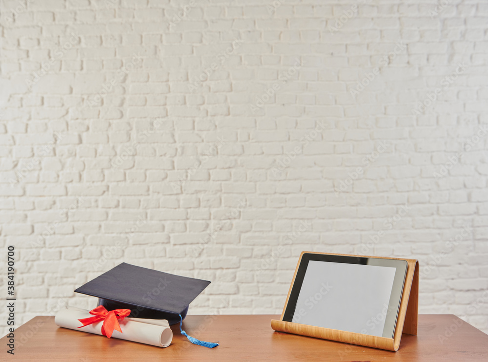 Graduated cap and laptop on the wooden table, white brick background ...