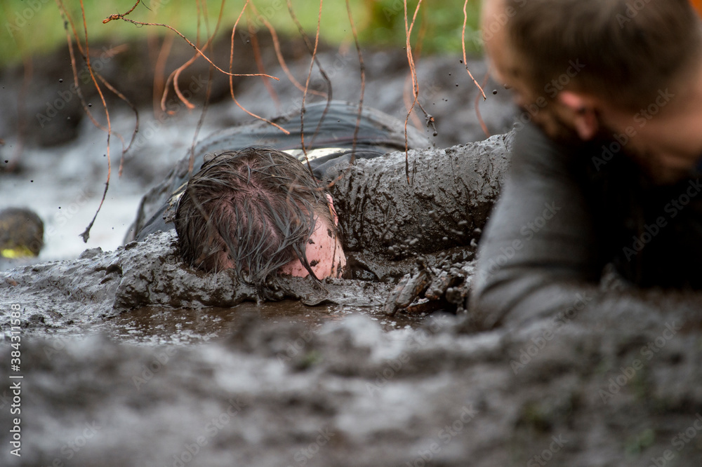 Mud race runners. Crawling,passing under a barbed wire obstacles during ...
