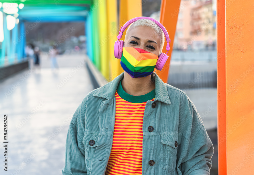 Young woman wearing gay pride mask while listening to music with ...