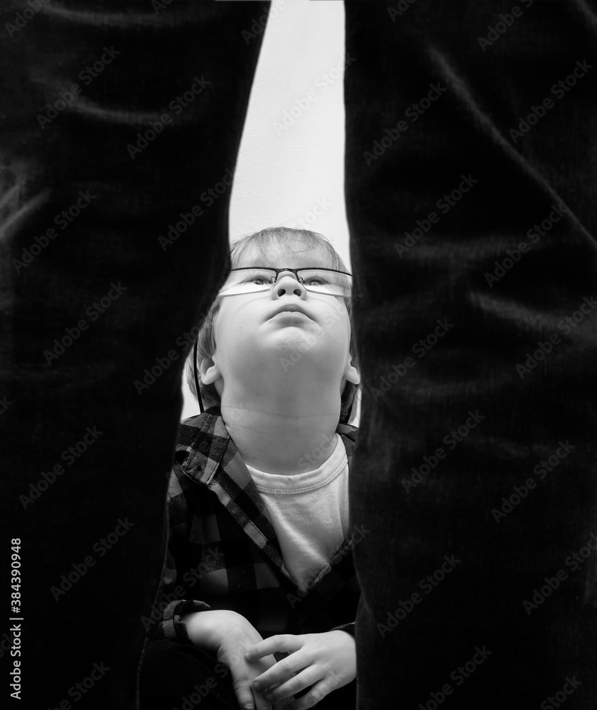 A little boy with glasses is sitting and looking up at the standing man ...