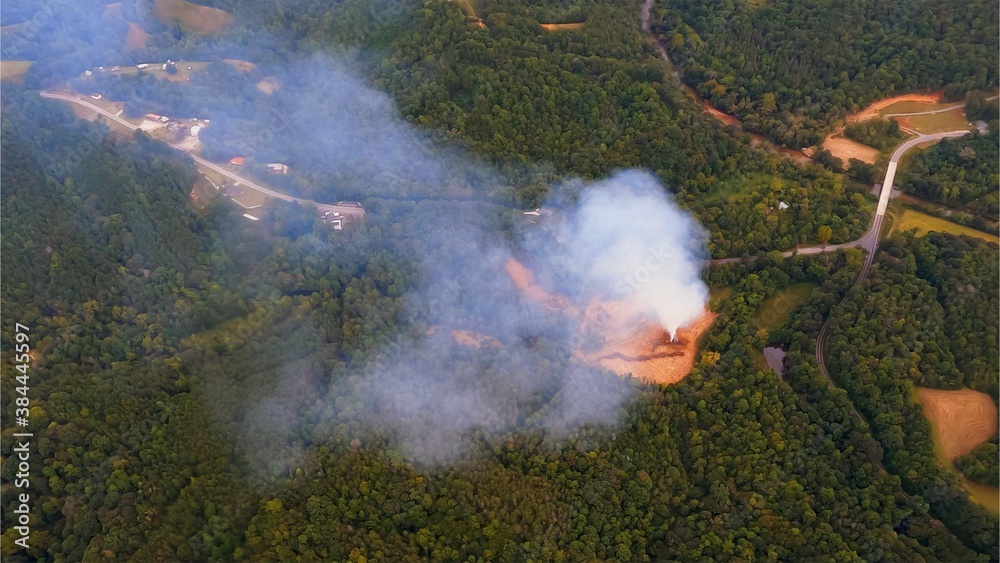 As I fly over a heavily forested area we see a small fire with a lot of ...