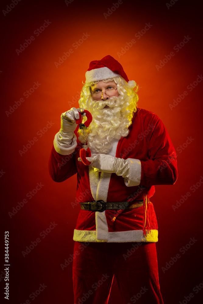 Male actor in a costume of Santa Claus holds red fur handcuffs and a ...