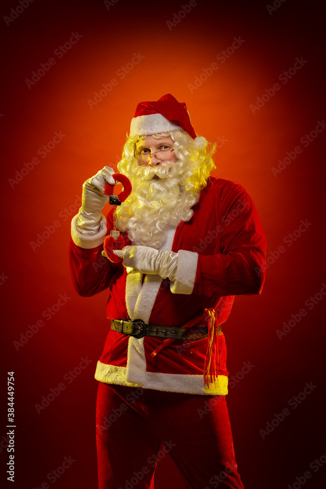 Male actor in a costume of Santa Claus holds red fur handcuffs and a ...
