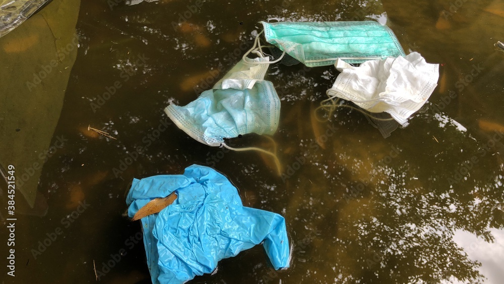 Used infectious masks and medical glove floating in dirty water,dimly ...