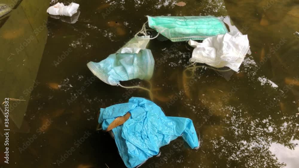 Used infectious masks and medical glove floating in dirty water,dimly ...