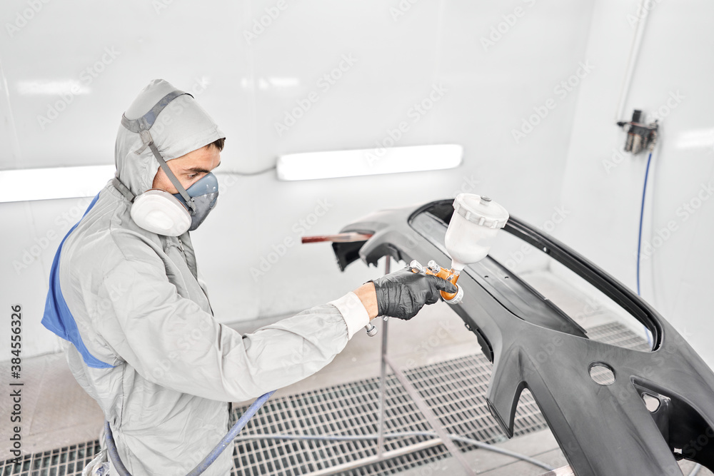 Worker painting parts of the car in special painting chamber, wearing ...