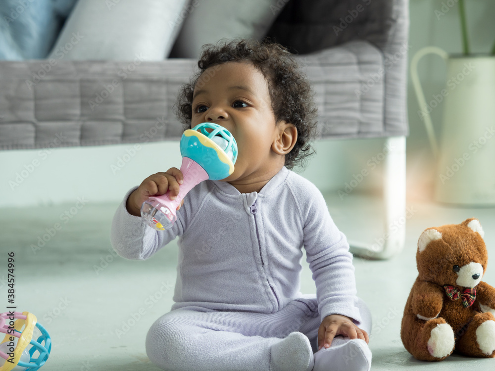 Cute little Black baby boy putting rattle toy into mouth. Stock Photo ...