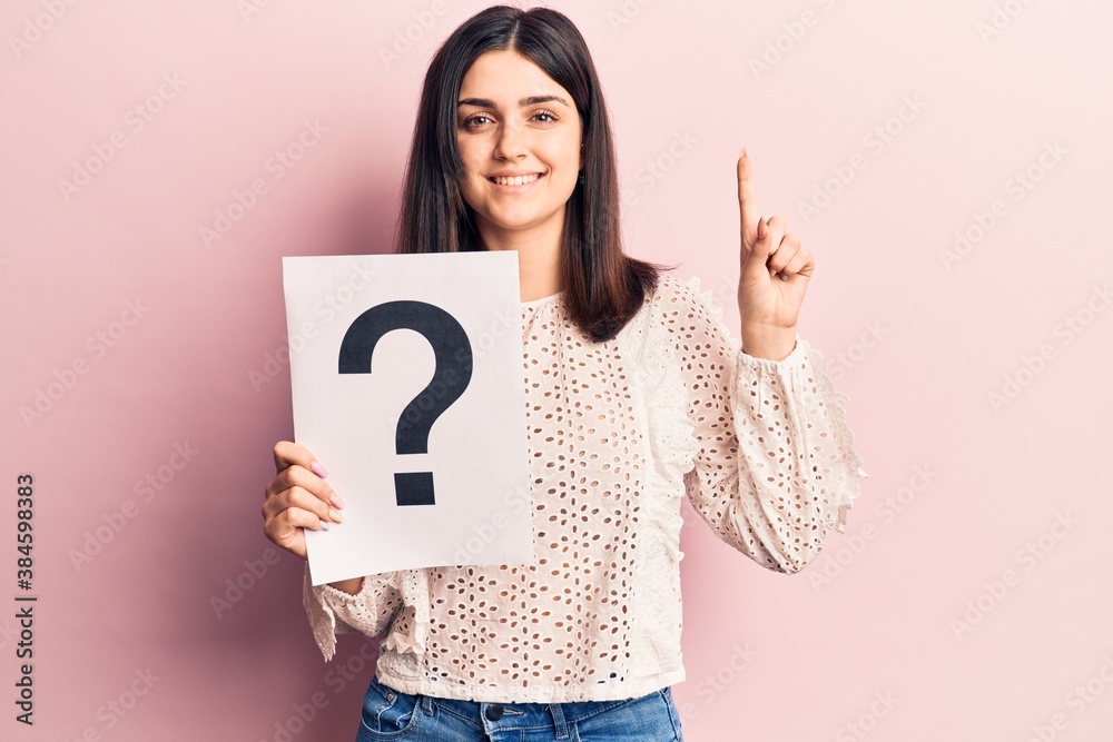 Young beautiful girl holding question mark smiling with an idea or ...