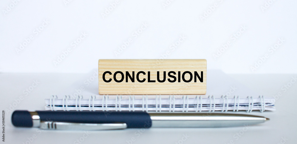 The word Conclusion on a bar of jenga wood, lying on a Notepad with a ...