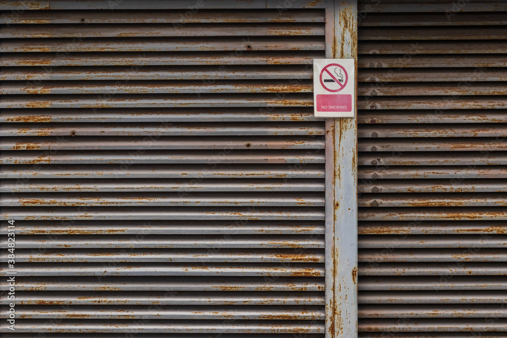 Old rusty and dust metal shutter doors with no smoking sign in the abandoned gas station ...
