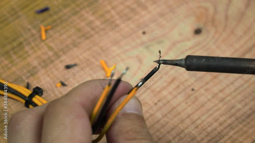 a man soldering wires with a soldering iron with smoke. He solders each ...