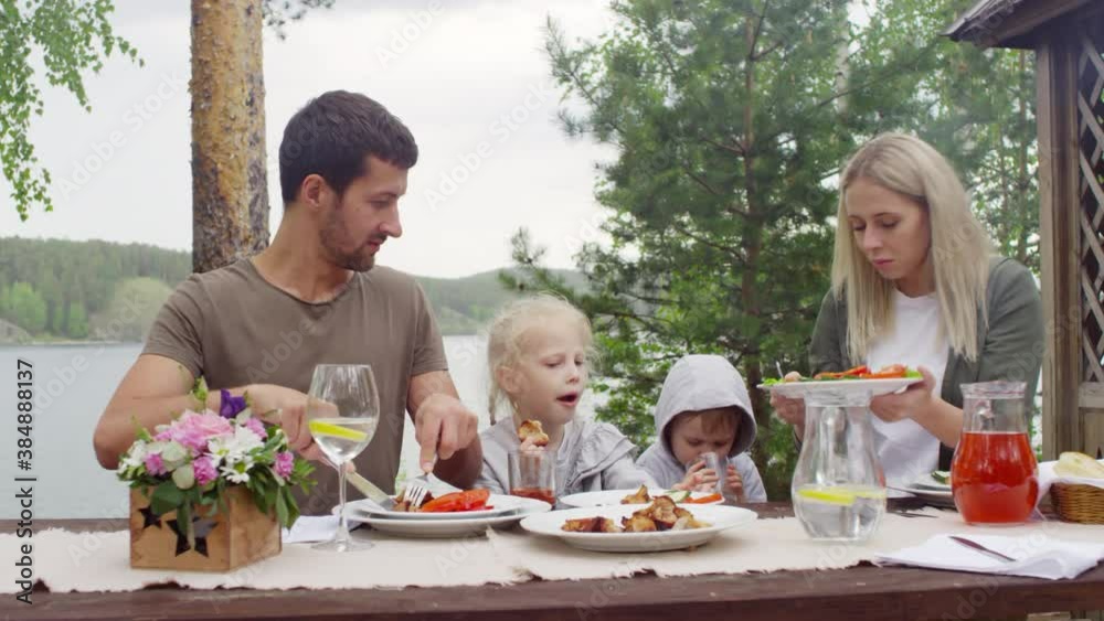 Tracking shot of happy family of four sitting at picnic table and ...