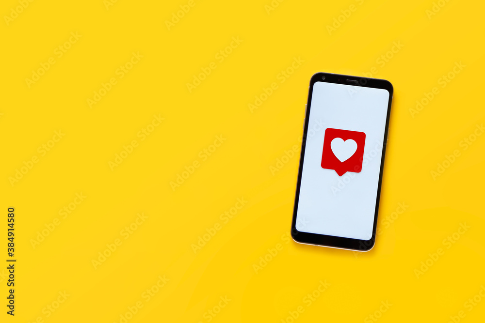 Top view of cell phone with heart emoticon. White screen and yellow ...