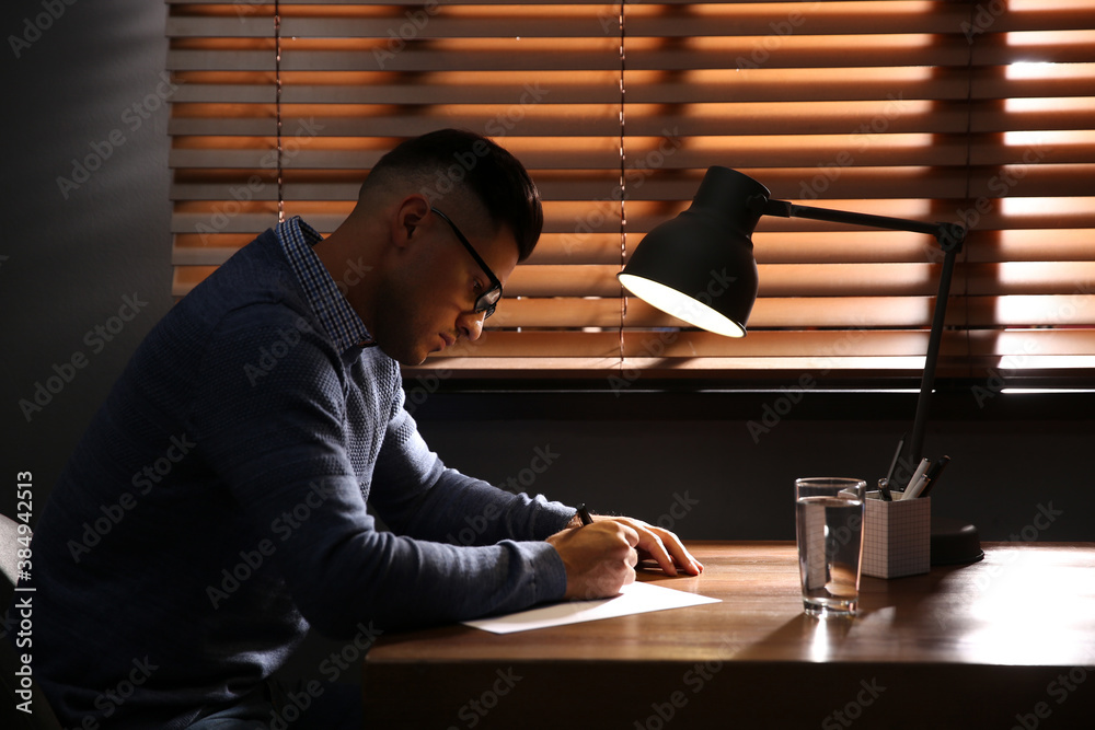 Man writing letter at wooden table in dark room Stock Photo | Adobe Stock