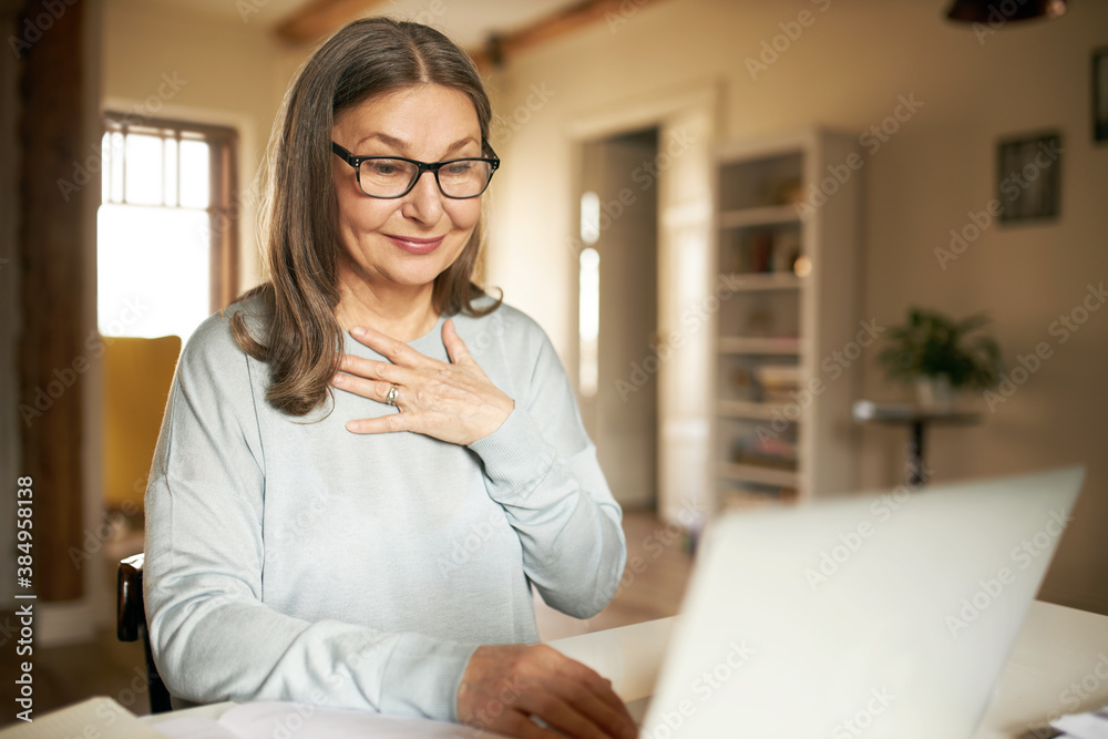 Emotional senior woman in glasses using portable computer reading ...