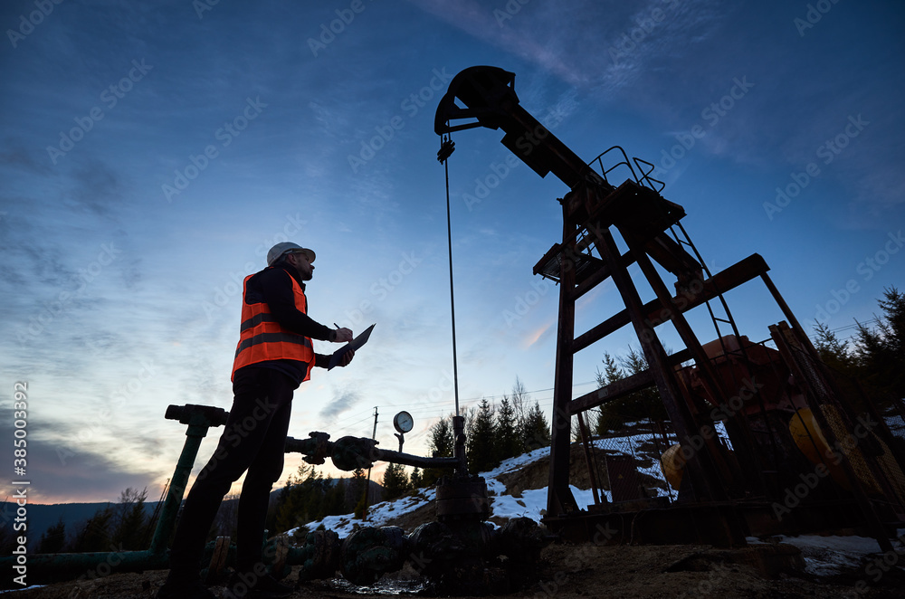 Low angle side view snapshot of petroleum engineer wearing orange vest ...