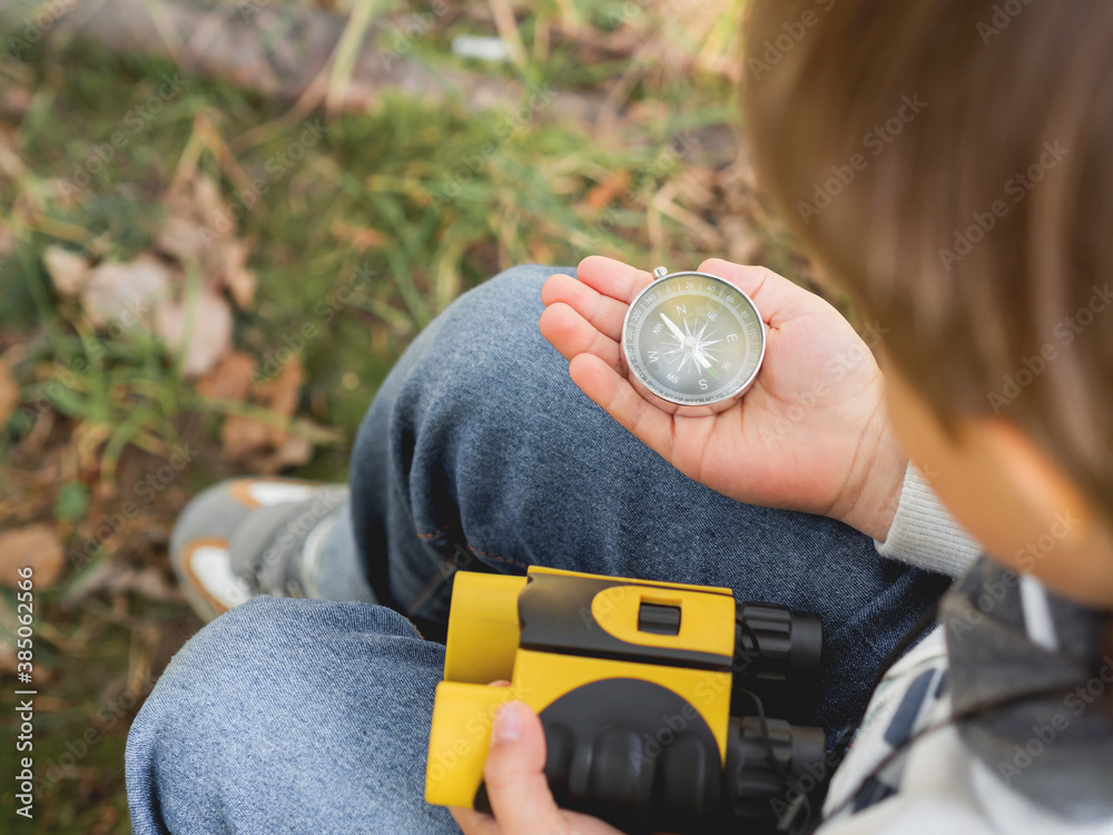 Little explorer on hike in forest. Boy with binoculars and compass sits ...