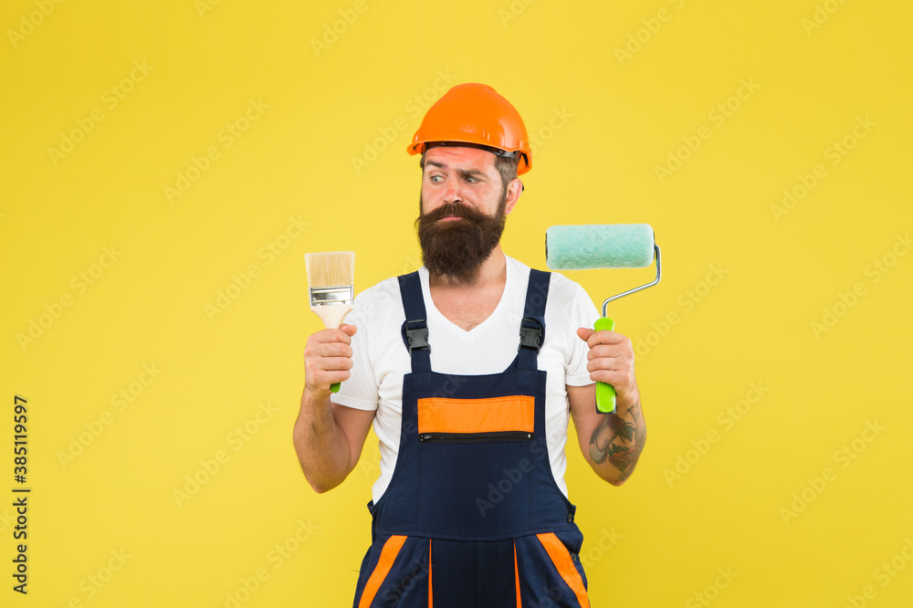 Skilled painter with serious look in working overalls hold paint brush ...